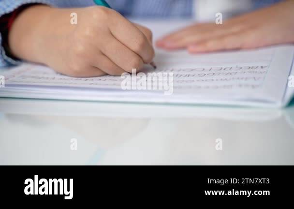 Elementary school student boy or girl writing letters, studying at desk ...