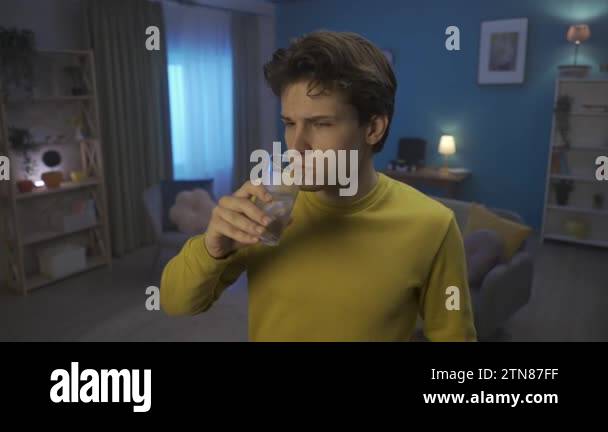 A man drinks ice water while standing in the living room close up. The ...
