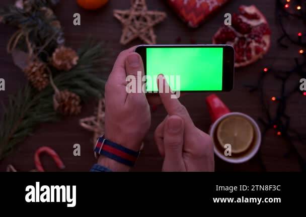 Christmas top view. Man hand holding smart phone with green screen ...