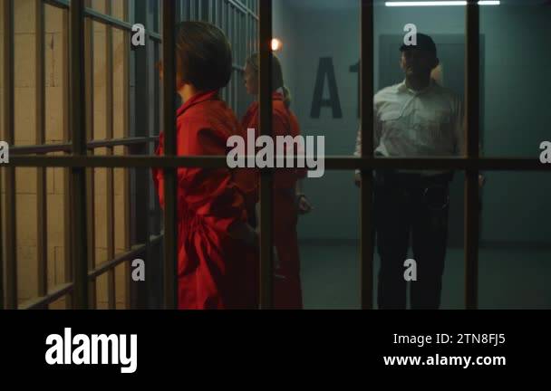 Two female prisoners, inmates in orange uniforms stand facing the metal ...
