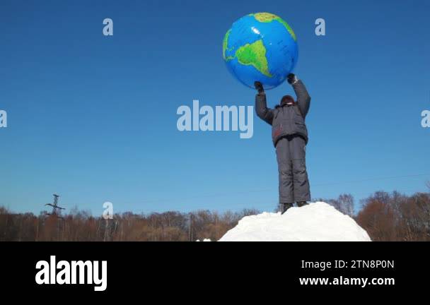 Boy stand on snow pile and hold inflated ball over head, then he throws ...