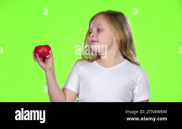 Little girl looks at a tomato, admires it and shows a thumbs up. Green ...