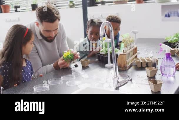 Diverse male teacher and happy schoolchildren studying plants in school ...