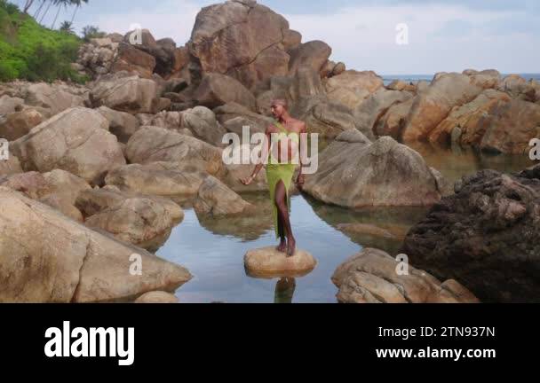 LGBTQIA black person in luxury dress poses on rock at lake on stunning ...