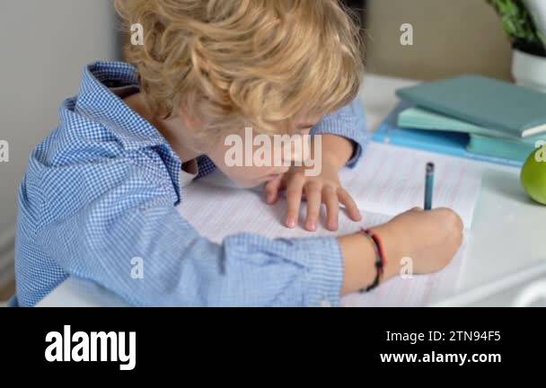 Elementary school student boy or girl writing letters, studying at desk ...