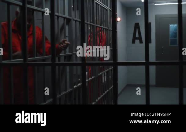 Prisoners in orange uniforms hold metal bars in jail. Guilty criminals ...