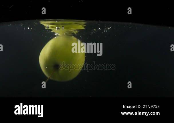 Closeup of fresh green apple falling into water on the black backgrond ...
