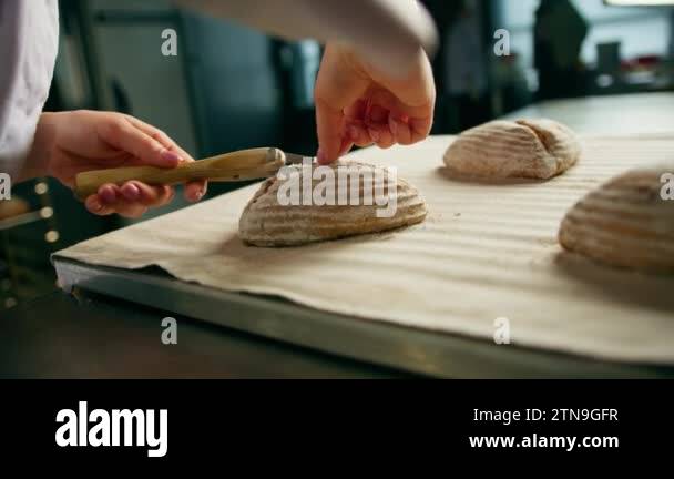 woman baker cuts patterns on raw bread rolls with a professional baker ...