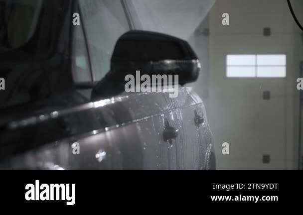 Car wash and detailing. A professional worker washes a black car with a ...