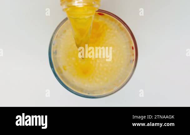 Orange drink is poured into a glass. A yellow liquid with gas bubbles ...