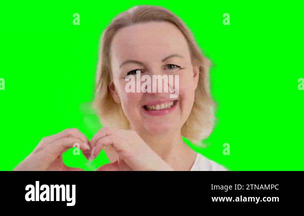 woman sincerely smiles with hands shows a heart squinting her eyes on a ...