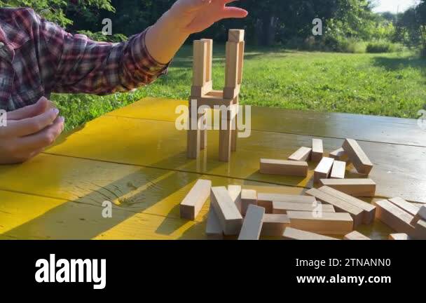 Adult woman builds tower with wooden blocks on yellow table outdoors at ...