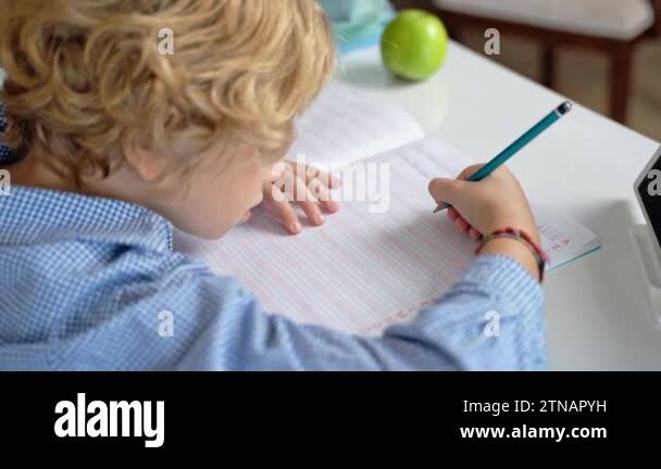 Elementary school student boy or girl writing letters, studying at desk ...