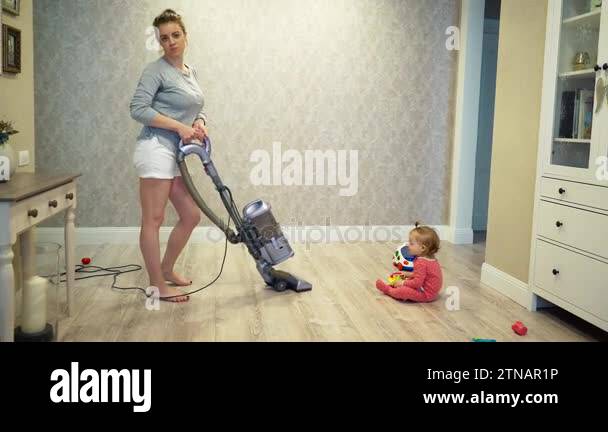 Mother clean dust from the floor with a vacuum cleaner and a little ...