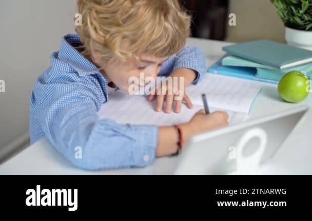 Elementary school student boy or girl writing letters, studying at desk ...