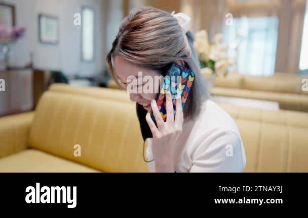 Engaged in conversation, a young Asian person holds a phone to their ...