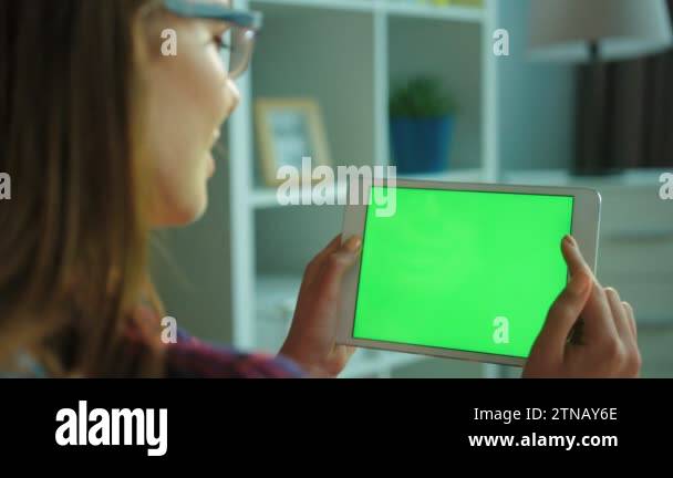 Young woman using white tablet computer with green screen while sitting ...