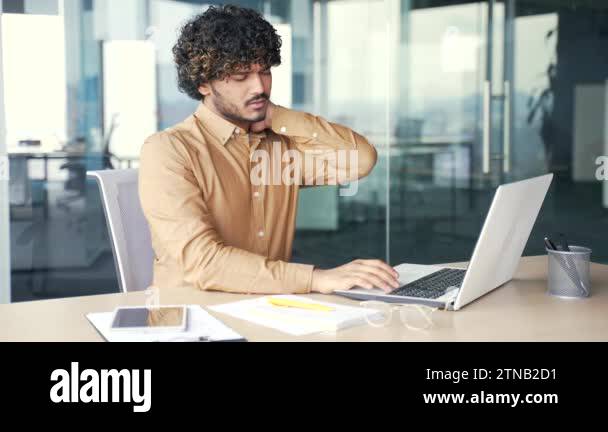 Tired young employee suffering from neck pain while working on laptop ...