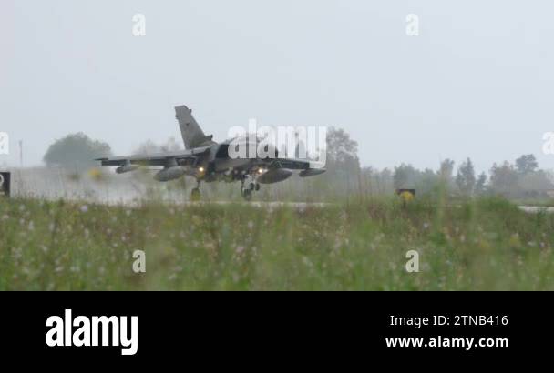 NATO bomber lands on a wet runway hidden by tall grass. Aircraft thrust ...