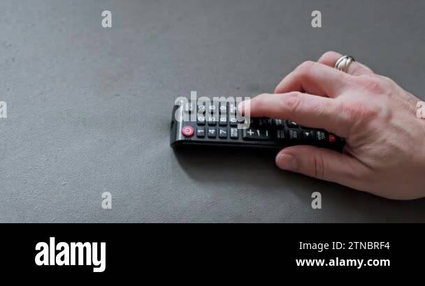 The TV remote control is used by a man. The mans hand quickly presses ...