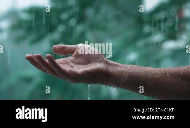 Rain drops falling on mans hand during the rainy day on green nature ...