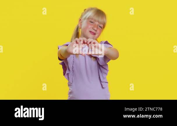 I love you. Smiling young cute blonde school girl makes heart gesture ...