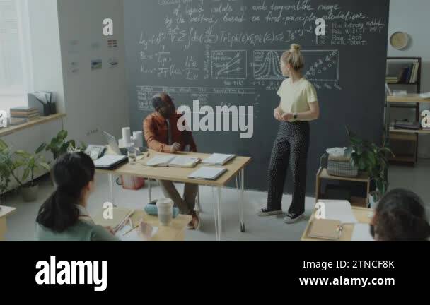 Tilt down shot of college girl standing by chalkboard in classroom and ...