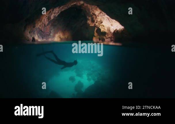 Freediver swims underwater in the cave. Male freediver explores the ...