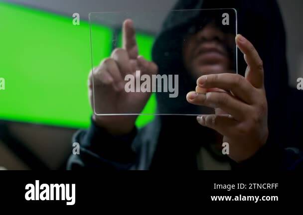 Hacker using clear glass tablet with green screen monitor behind and ...