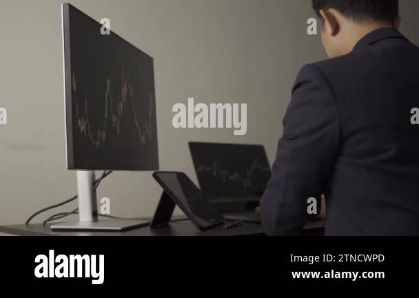Side view of young asian male stockbroker analyzing charts on multiple ...