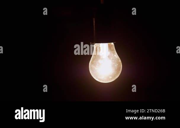 Hanging Swinging Glowing Light Bulb in a Dark Room on the Black ...