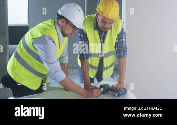 Engineer and Worker Bending over Large Blueprint and Having Conversation, inside Building Under ...