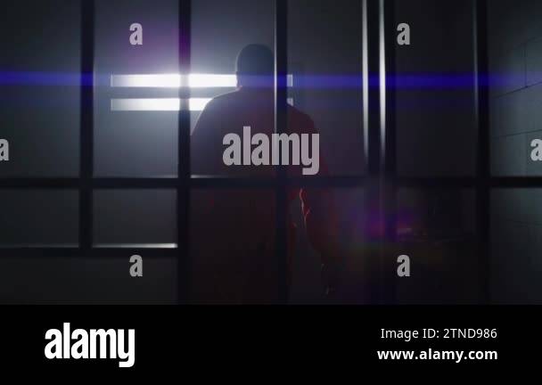 Depressed African American man in orange uniform stands from jail bed ...