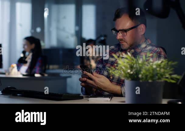 Late Night at the Office. Man Sits at His Desk, Consults Smartphone ...