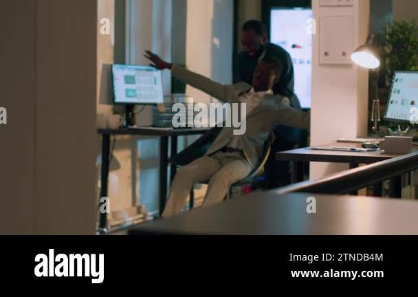 African american employee sliding with chair in office hallway ...