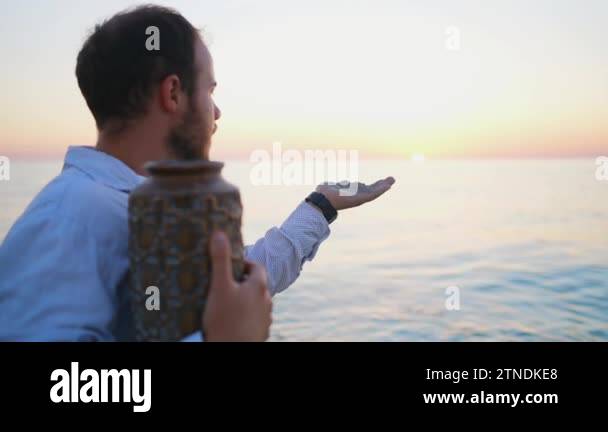 man blows ashes from the palm of his hand with ashes from a cremation ...