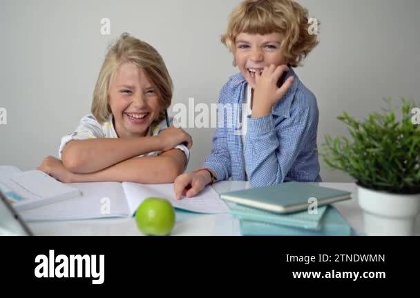 Primary elementary middle school boy girl siblings studying at desk table, writing in book and ...