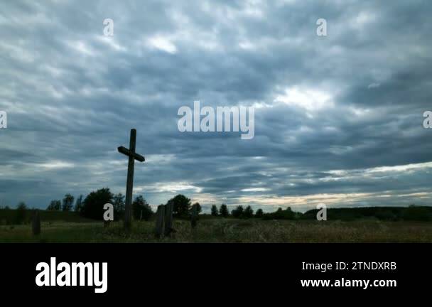 Wooden cross in the field above the dramatic sky with clouds. Time ...
