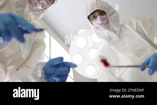 Two doctors wearing masks and protective suits hold scalpel and forceps ...