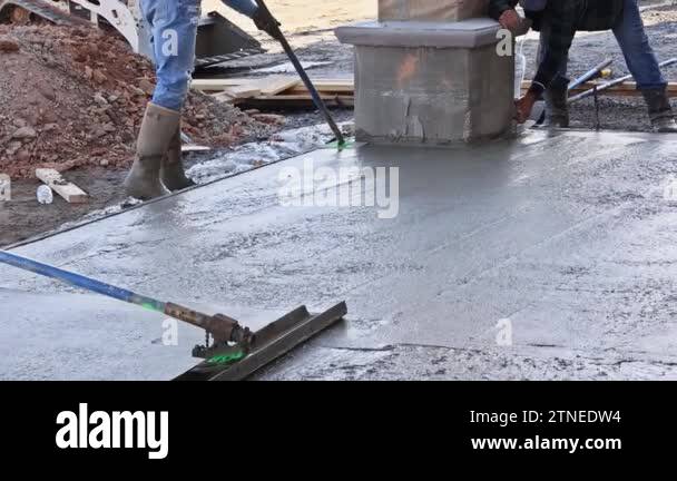 In construction site, workers are leveling concrete for driveway with ...
