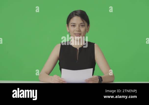 An Asian TV presenter sits at a table and reads information from a ...