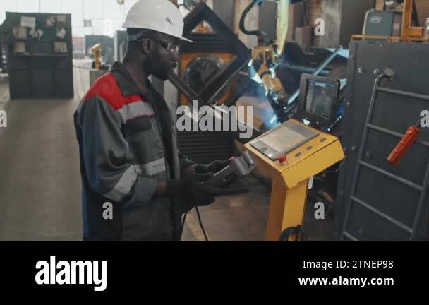 Black male plant worker using teach pendant robotic manipulator while ...