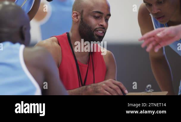 Diverse male basketball team and coach with clipboard in discussion at ...