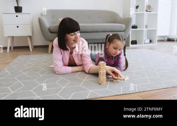 Attentive preteen girl putting block in tumble tower while calm adult ...