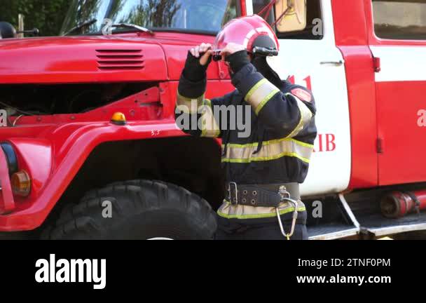 Young fireguard taking off helmet and balaclava stands near fire engine ...