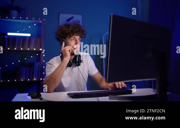 Gamer guy sitting at the computer at night and uses a smartphone ...