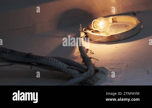 An incandescent light bulb glows in an old broken lamp on the concrete ...