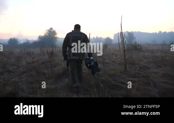 Male firefighter in uniform going on dry grass at countryside ...