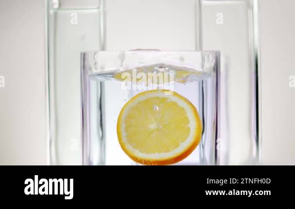 slice of lemon falls into the water in a glass container on a white ...