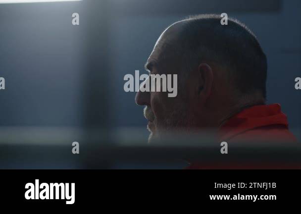 Elderly criminal in orange uniform sits in jail cell and looks on ...